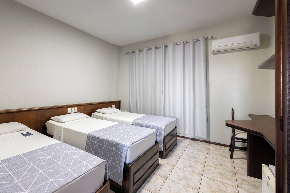 Quarto de hotel com duas camas, uma escrivaninha e um ar condicionado.