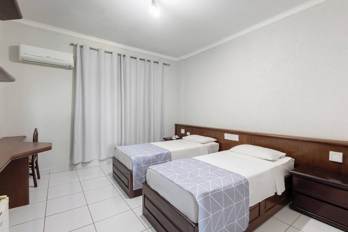 Quarto de hotel com duas camas, uma escrivaninha e uma cadeira.