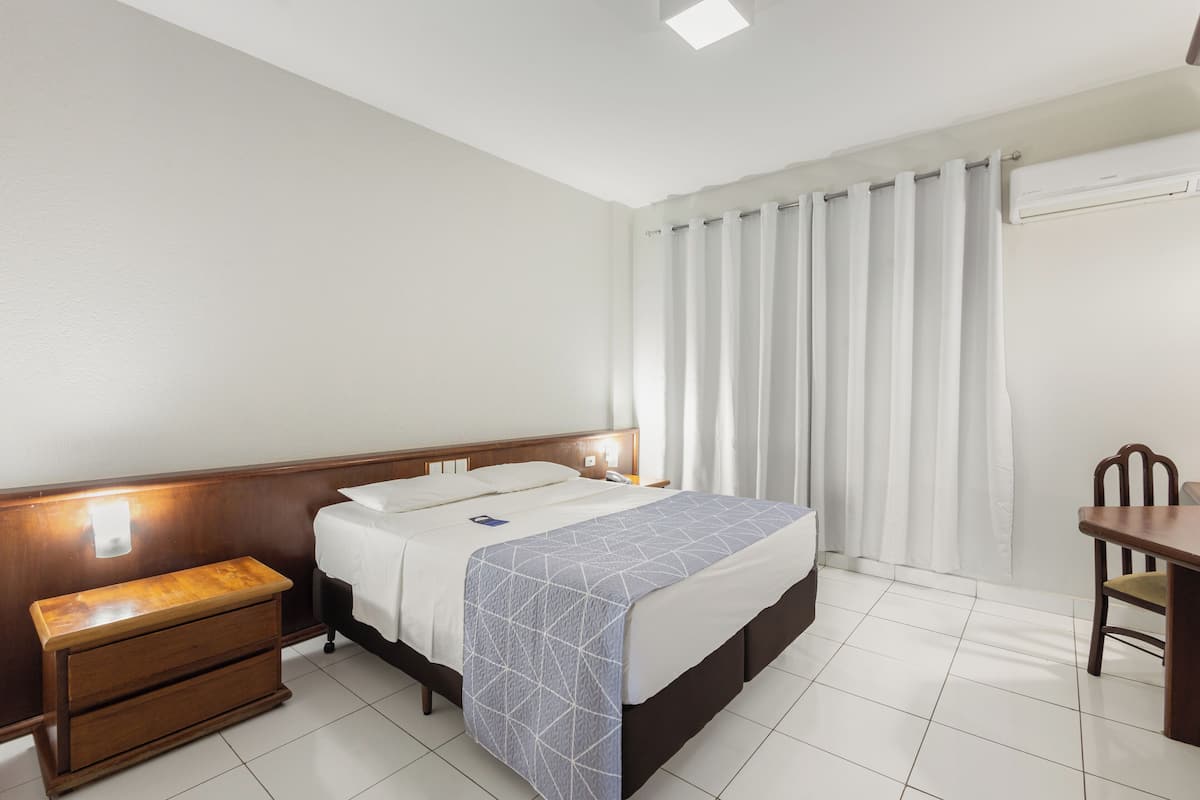 Quarto de hotel com cama, mesa de cabeceira e escrivaninha com cadeira.