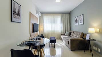 Quarto de hotel moderno com área de refeições, sofá e televisão presa à parede.