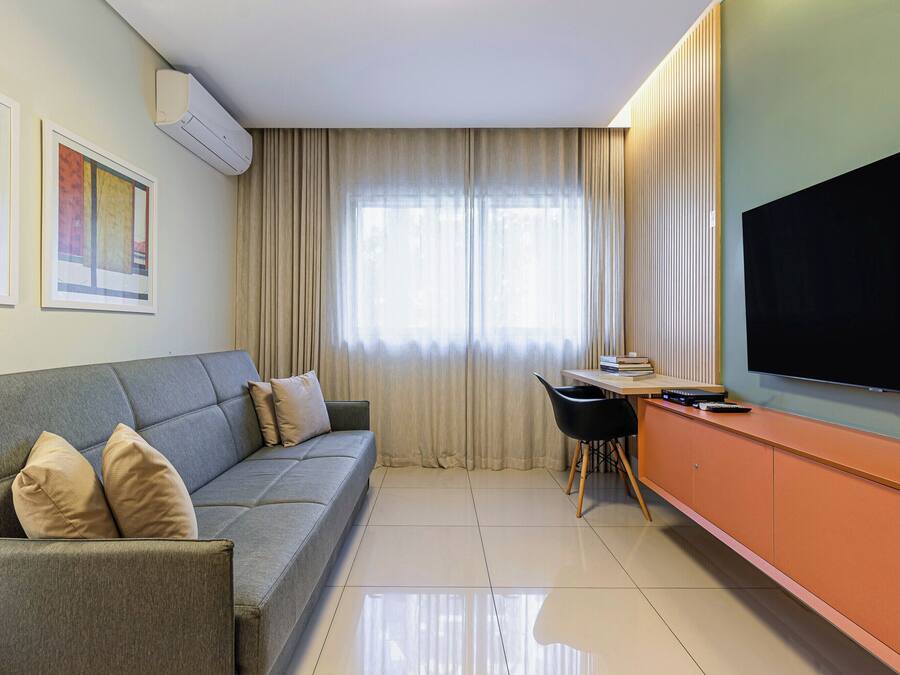 Uma sala de estar moderna com um sofá, uma televisão, um espaço de refeições e uma janela com cortinas.
