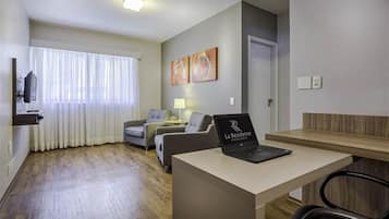Quarto de hotel com escrivaninha, duas cadeiras, televisão, luminária e obras de arte na parede.
