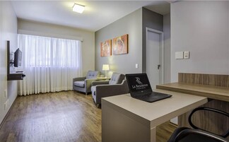 Quarto de hotel com escrivaninha, duas cadeiras, televisão, luminária e obras de arte na parede.