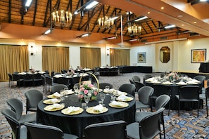 Uma sala de banquetes com mesas redondas dispostas para refeições, com toalhas de mesa pretas, jogos americanos dourados e arranjos florais.