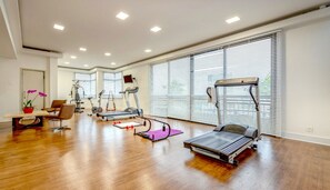 Uma academia ampla com diversos equipamentos de ginástica, grandes janelas e piso de madeira.