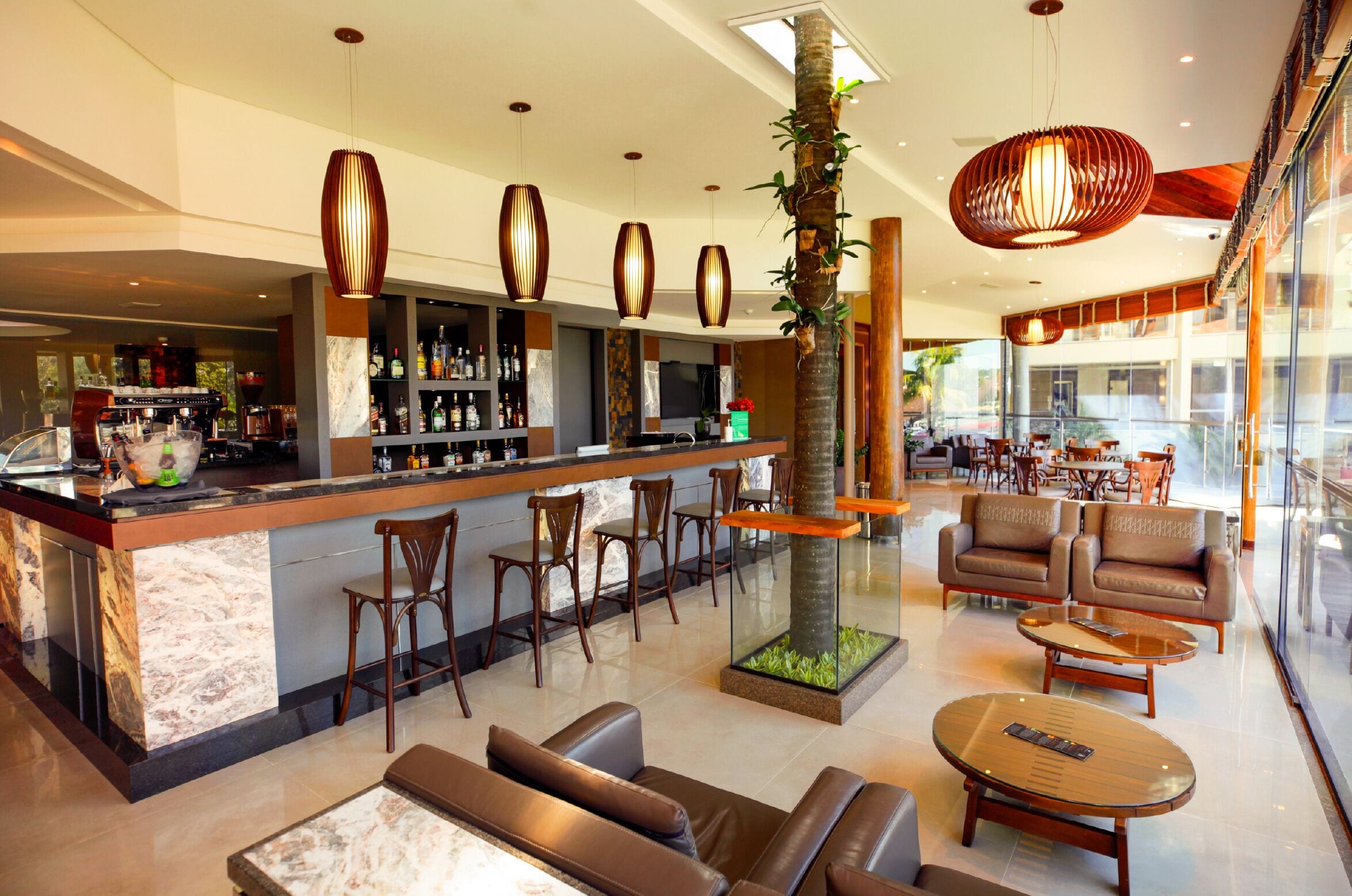 Uma área de bar com bancada de mármore, banquetas e uma luminária pendente grande.