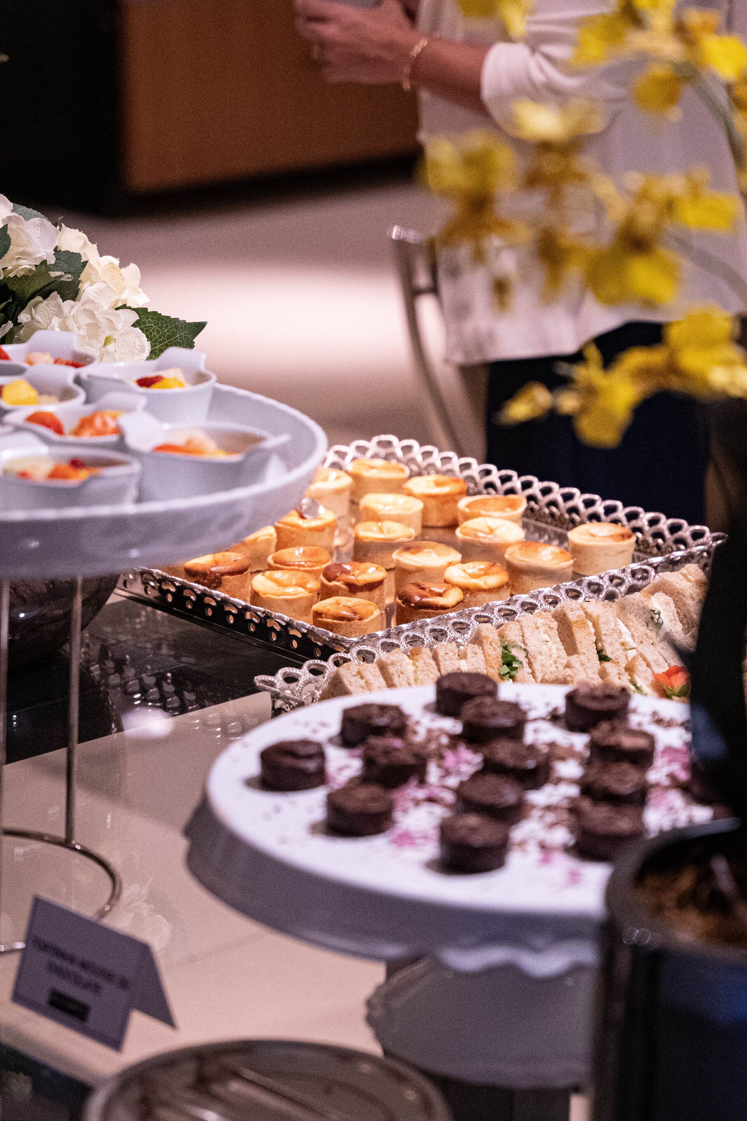 Buffet com diversos itens, incluindo pastéis, sanduíches e sobremesas.