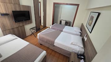 Quarto de hotel com duas camas, uma televisão na parede, uma mesinha e um quadro pendurado na parede.