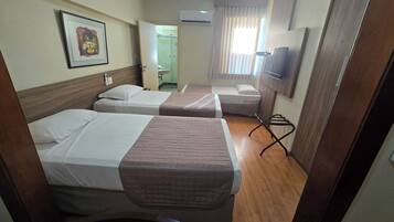 Quarto de hotel com duas camas, uma mesa pequena, uma televisão e um banheiro visível por uma porta aberta.