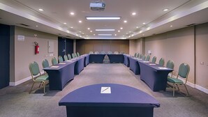 Uma sala de conferências com uma mesa comprida, cadeiras verdes e um projetor no teto.