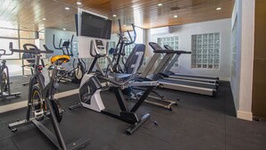 Uma academia com diversos equipamentos de exercícios, incluindo esteiras e bicicletas ergométricas, e um espelho grande que reflete o espaço.