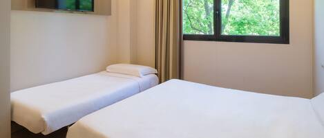 Quarto com duas camas individuais, televisão na parede e janela com vista para árvores.