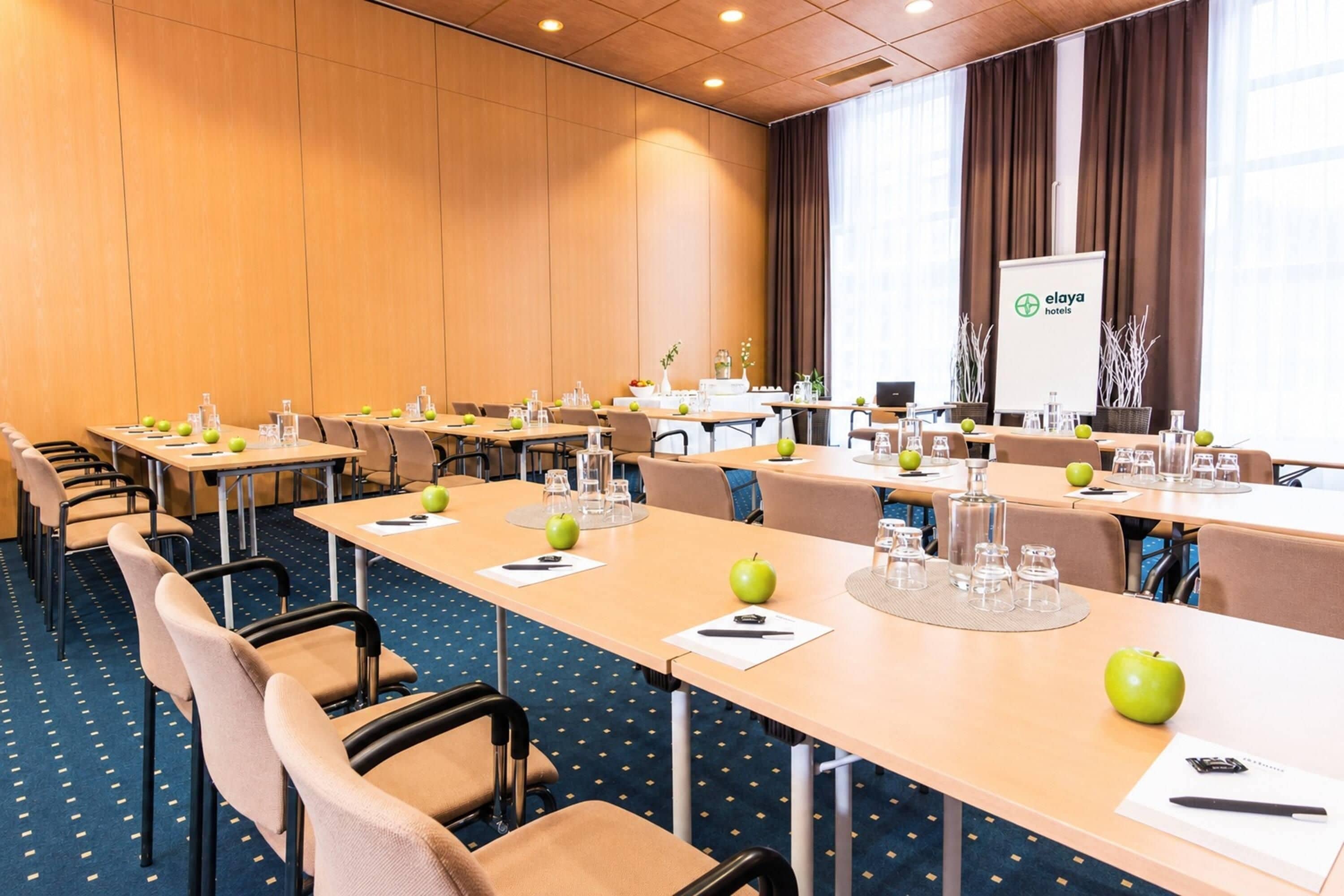 Sala de conferências com várias mesas, cadeiras e um ecrã de projeção.
