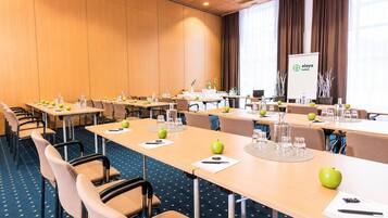 Sala de conferências com várias mesas, cadeiras e um ecrã de projeção.