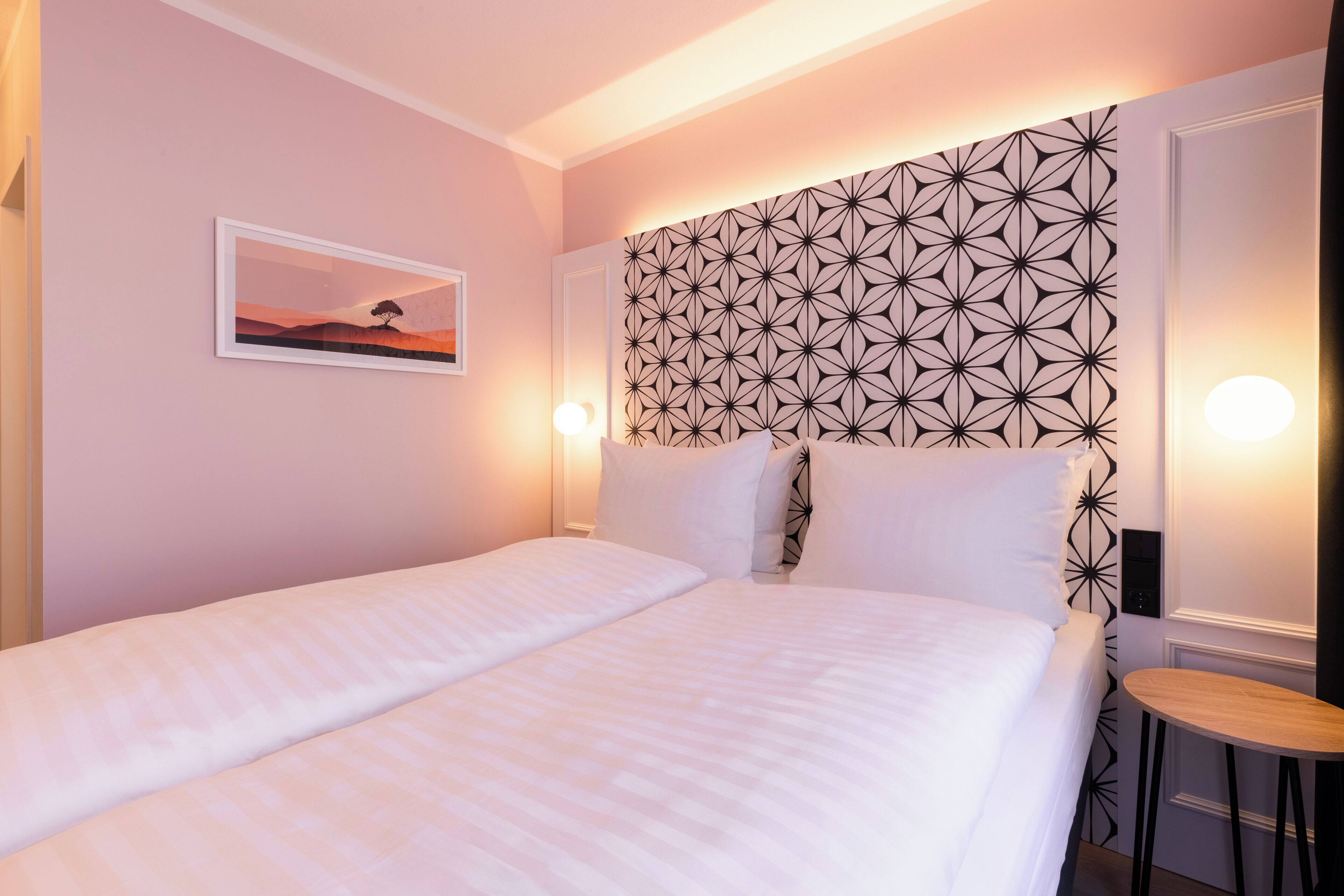 Quarto de hotel com uma cama grande, uma mesa pequena e uma parede com padrão geométrico.