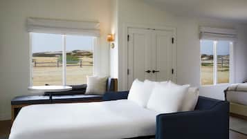 Quarto com cama, área de estar com mesa e duas janelas com vista para a praia.