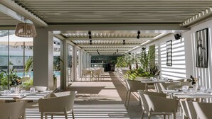 Um restaurante moderno com um amplo espaço para refeições, cadeiras e mesas brancas dispostas para jantares.