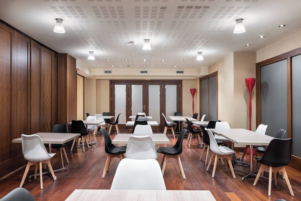Uma sala de conferências com várias mesas e cadeiras, painéis de madeira em uma parede e um teto com iluminação embutida.