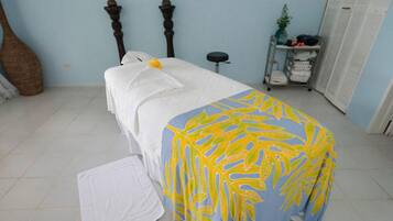 Quarto com uma cama, um banquinho, uma prateleira com objetos e uma parede com uma planta.