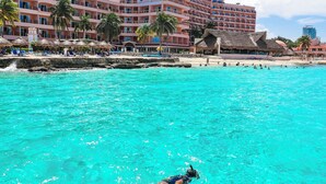 Uma pessoa nadando em águas turquesa cristalinas, com um prédio de resort ao fundo.