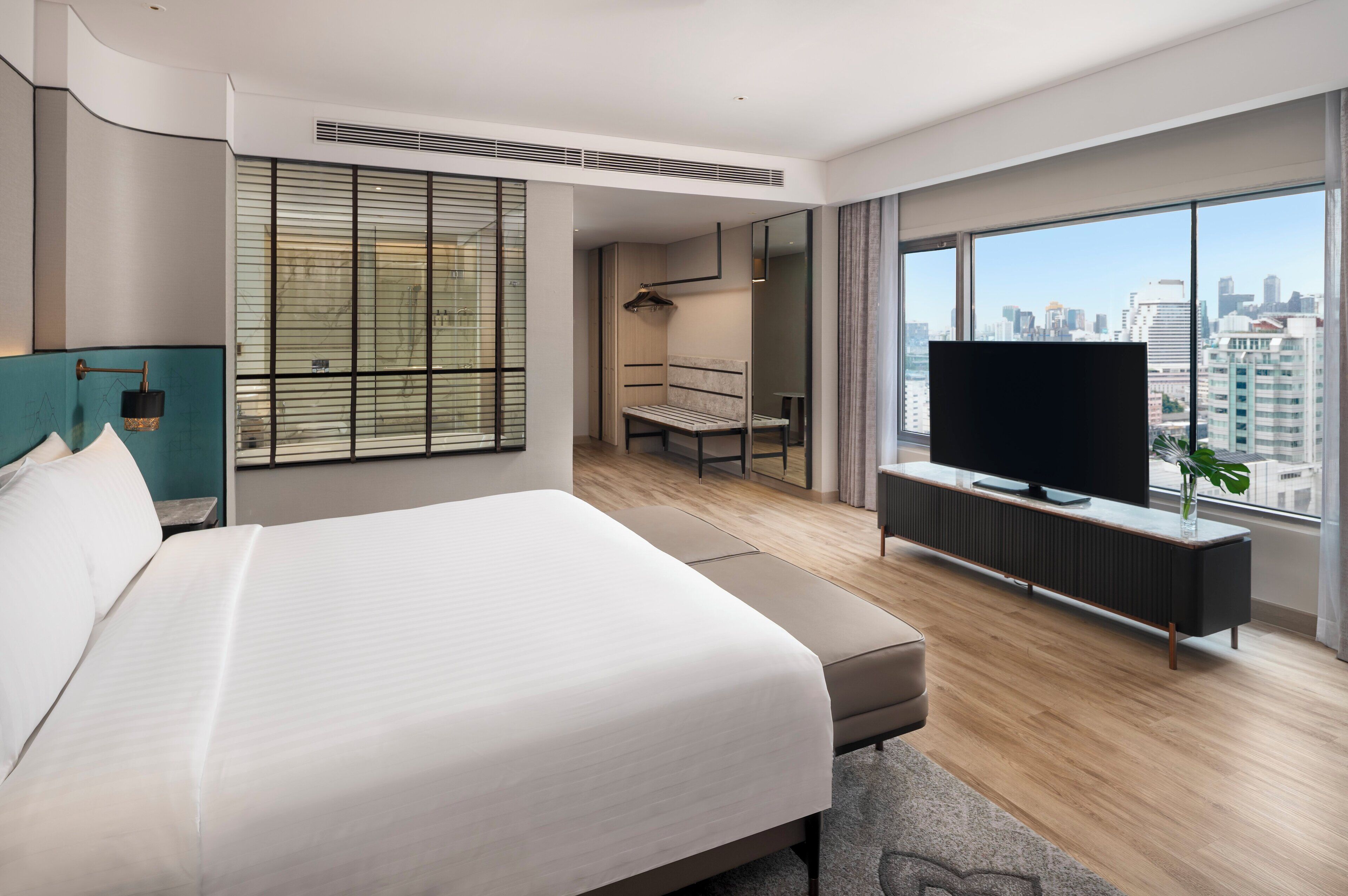 Quarto de hotel moderno com uma cama grande, área de estar, TV e vista para a cidade.