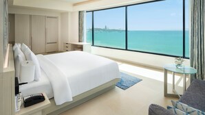 Quarto de hotel com uma cama grande, uma escrivaninha, uma cadeira e vista para o oceano.