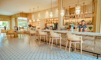 Uma área de bar com bancada de mármore, luminárias pendentes e diversos frascos e copos em prateleiras.