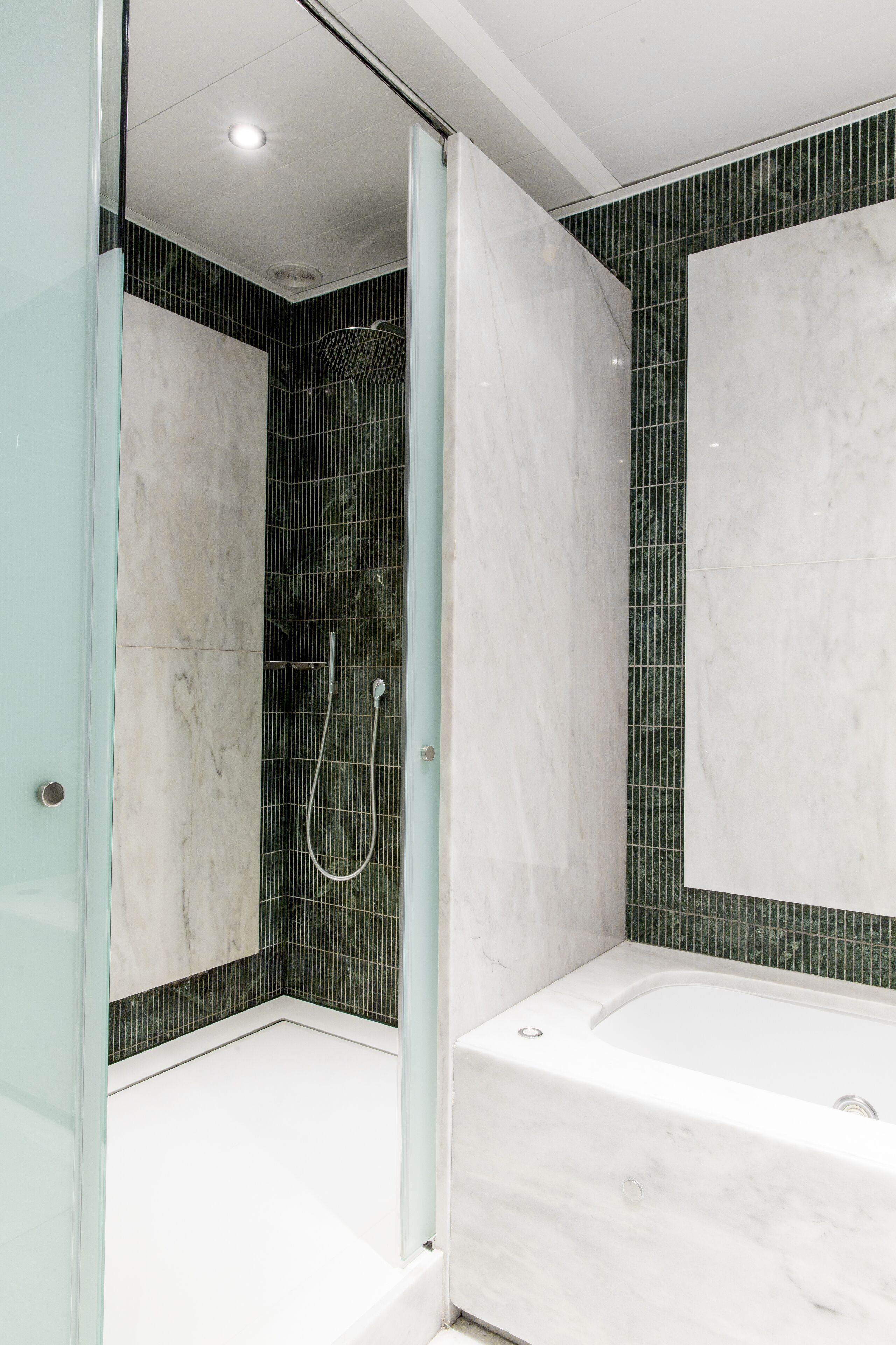 Uma casa de banho moderna com cabine de duche em vidro, uma banheira branca e paredes com azulejos verdes.