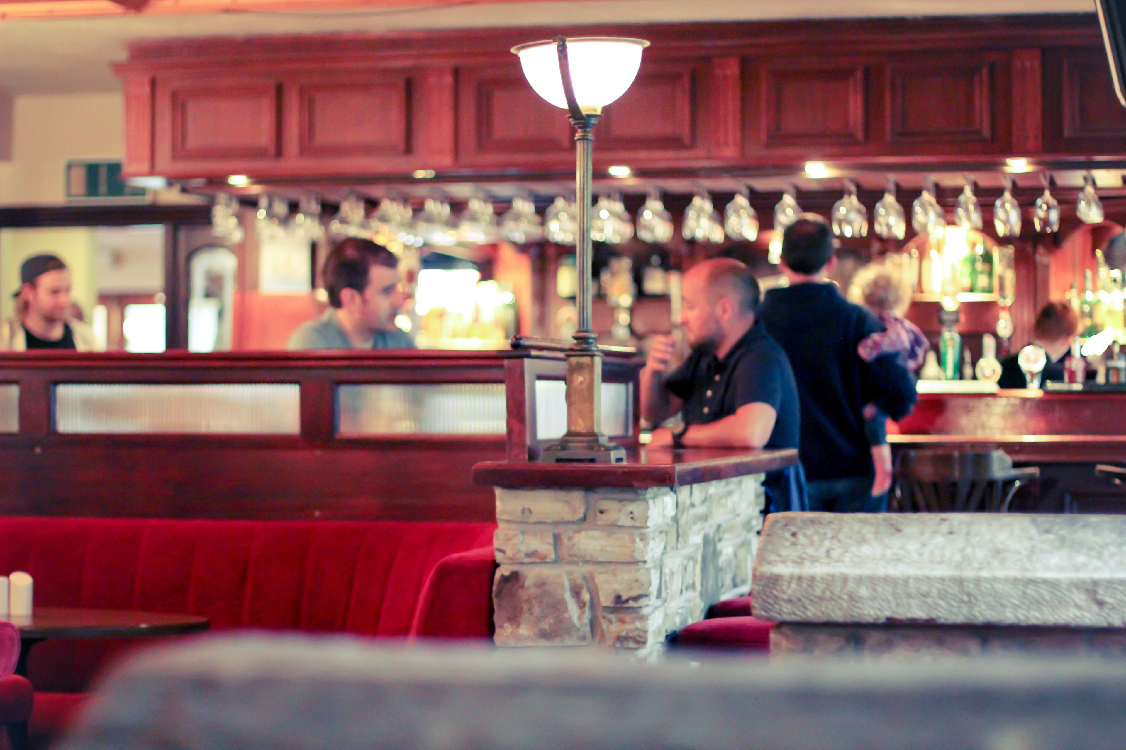 Uma área de bar com armários de madeira, um pilar de pedra e assentos vermelhos.