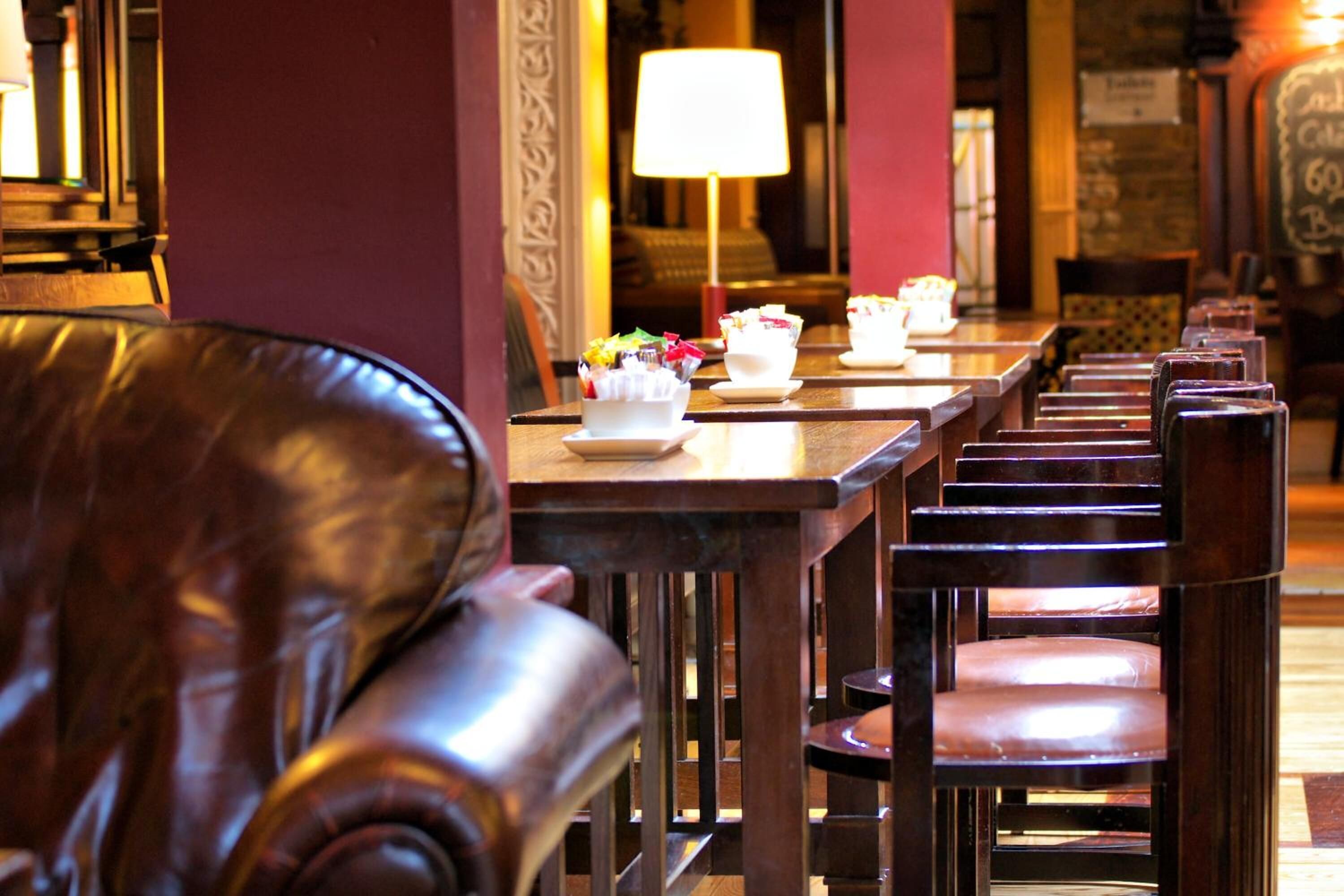 Um restaurante com mesas e cadeiras de madeira, um sofá de couro e um abajur.