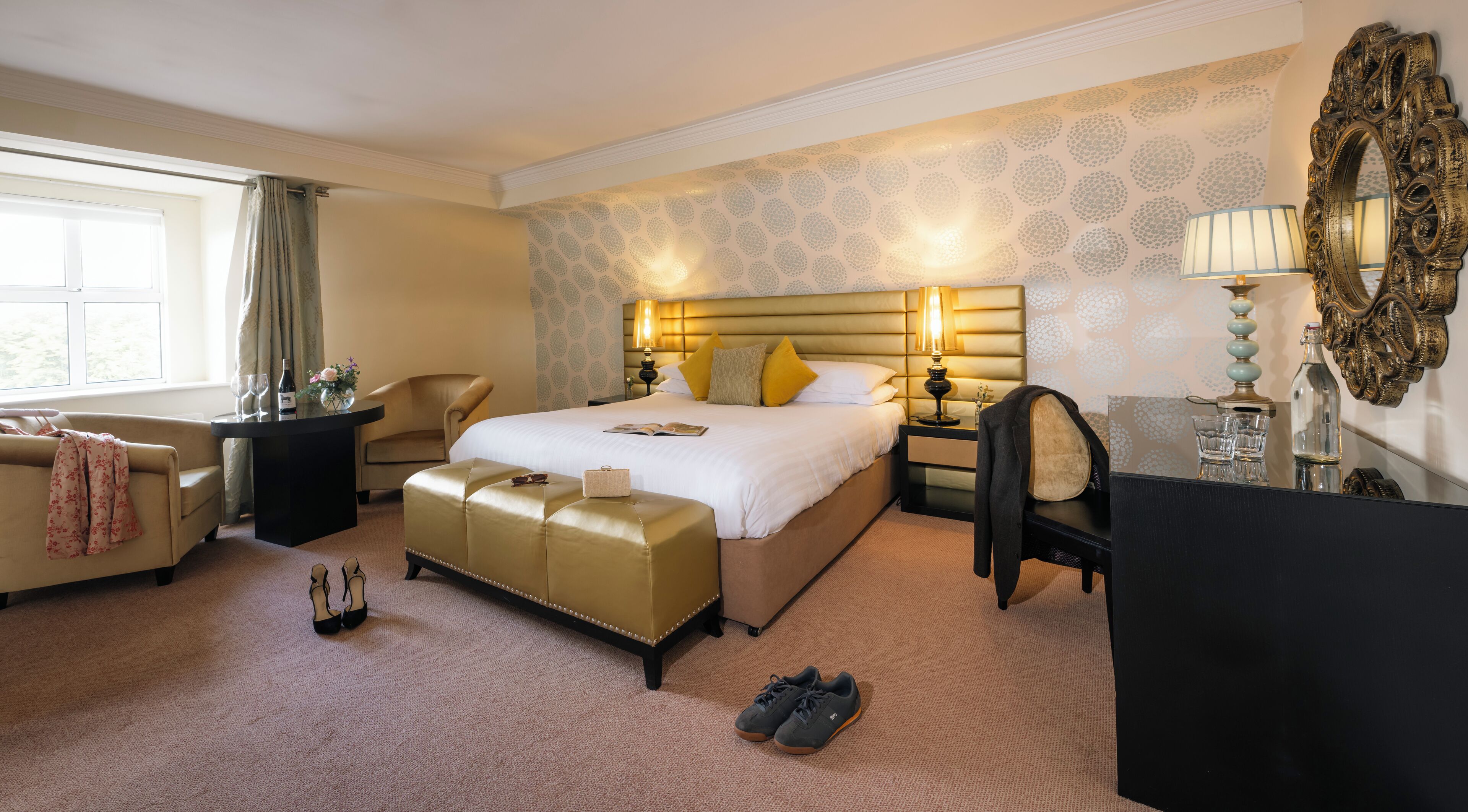 Quarto de hotel com cama, escrivaninha, cadeira, sofá e um espelho grande.