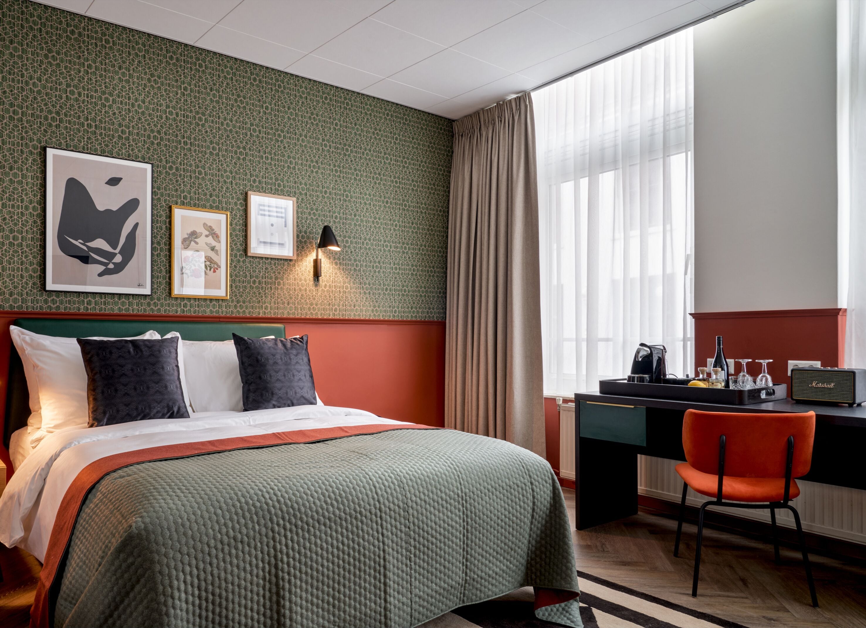 Quarto de hotel com cama, escrivaninha, cadeira e janela com cortinas.
