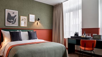 Quarto de hotel com cama, escrivaninha, cadeira e janela com cortinas.