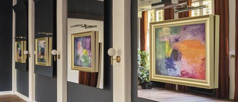 Um corredor com quadros abstratos emoldurados nas paredes, piso de madeira e teto com padrão de grade.