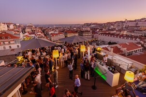 Um bar no terraço com gente, mesas ao ar livre e vista para a cidade.
