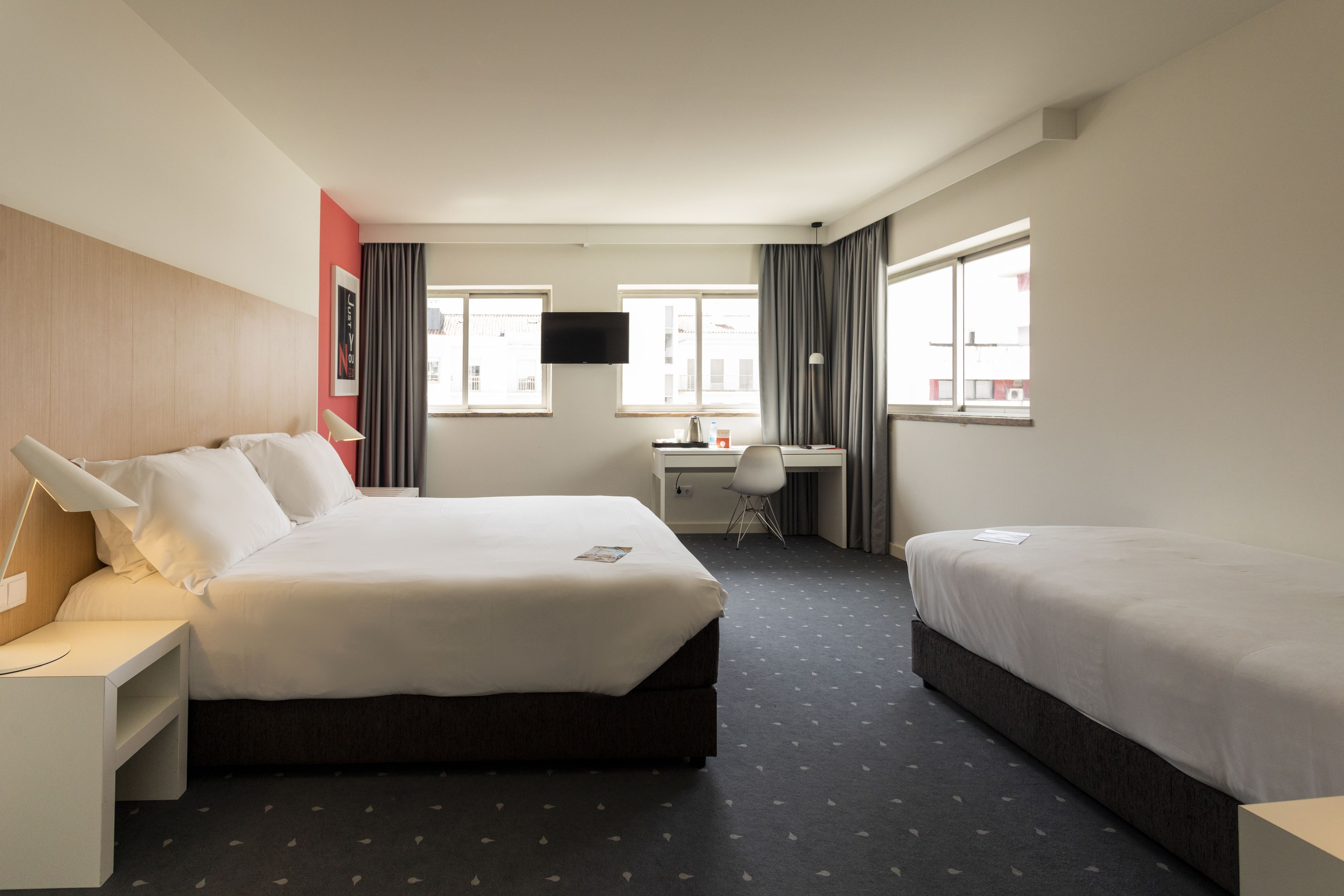 Quarto de hotel com duas camas, uma escrivaninha, uma cadeira e uma televisão.