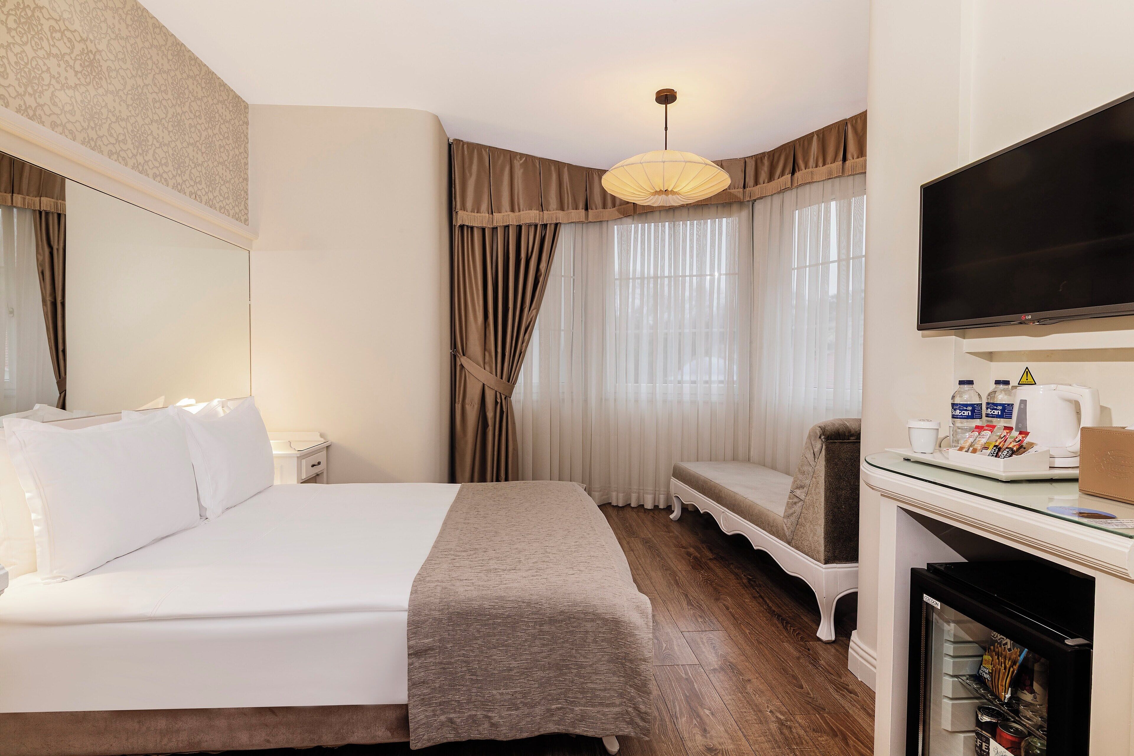 Quarto de hotel com cama, escrivaninha, televisão, cadeira e minibar.