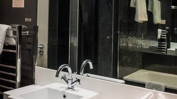 Casa de banho moderna com lavatório branco, cabine de duche em vidro e espelho a refletir um porta-toalhas e um lavatório.