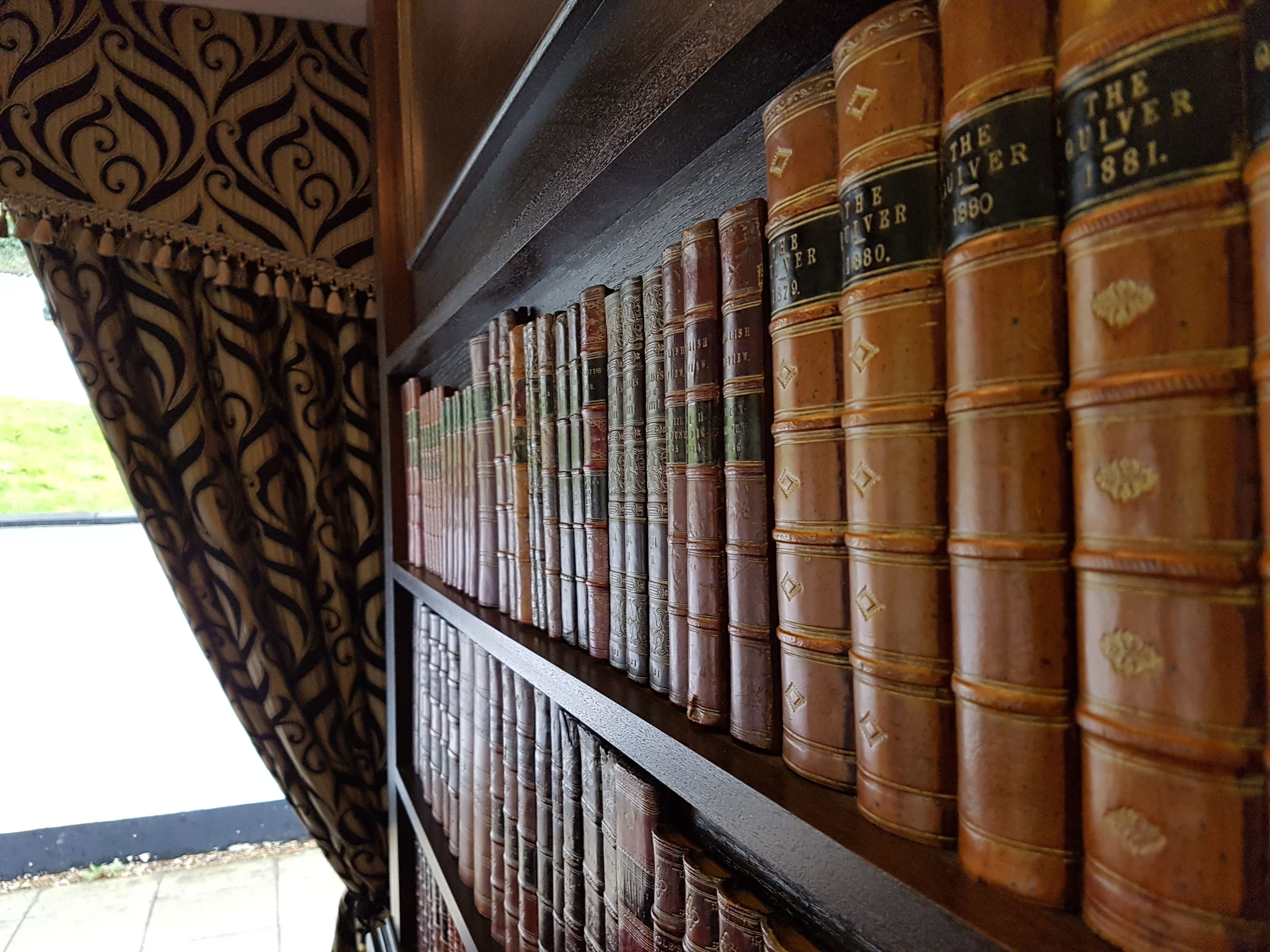 Uma estante com livros encadernados em couro, alguns com detalhes dourados, dispostos verticalmente.