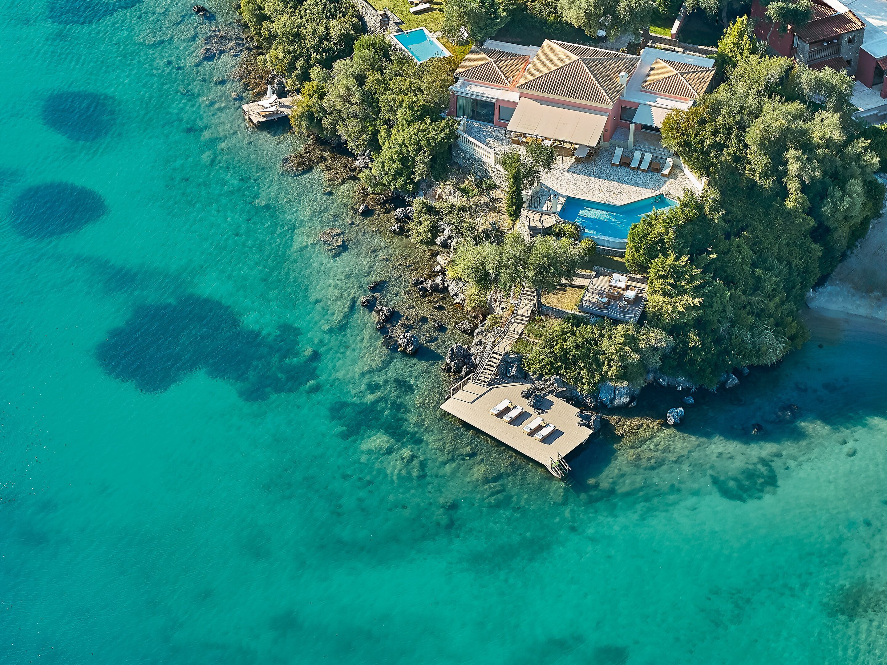Vista aérea de uma propriedade costeira com águas turquesa cristalinas, piscina e um píer.