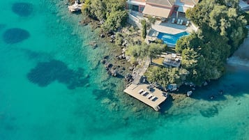 Vista aérea de uma propriedade costeira com águas turquesa cristalinas, piscina e um píer.