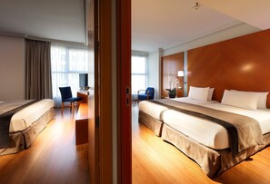 Quarto de hotel com duas camas, uma escrivaninha, uma cadeira e um vaso de planta.