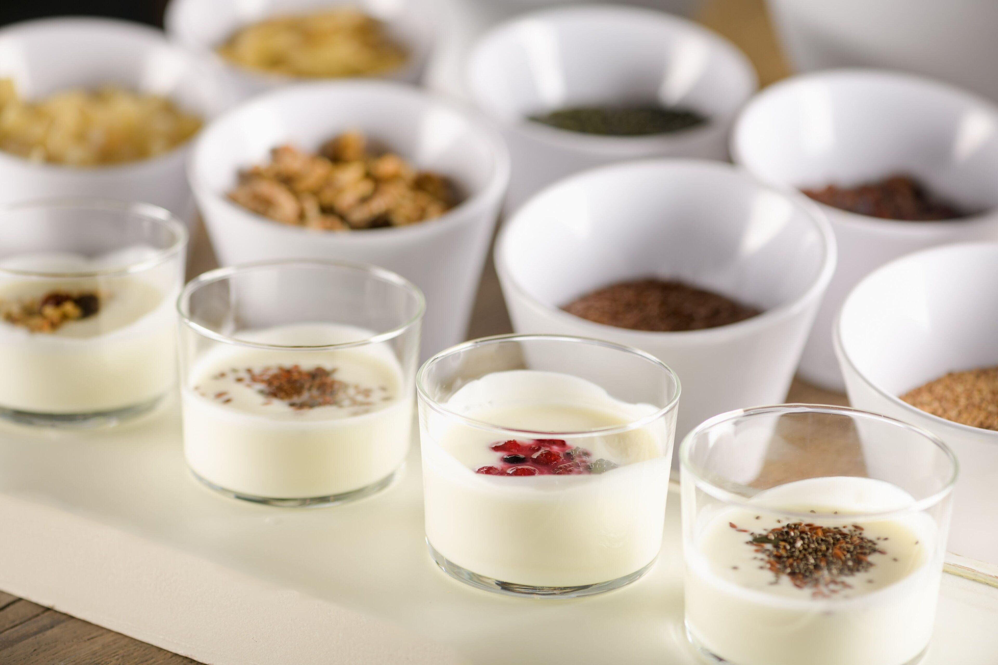 Três copos de iogurte com diferentes coberturas, rodeados por recipientes com vários ingredientes.