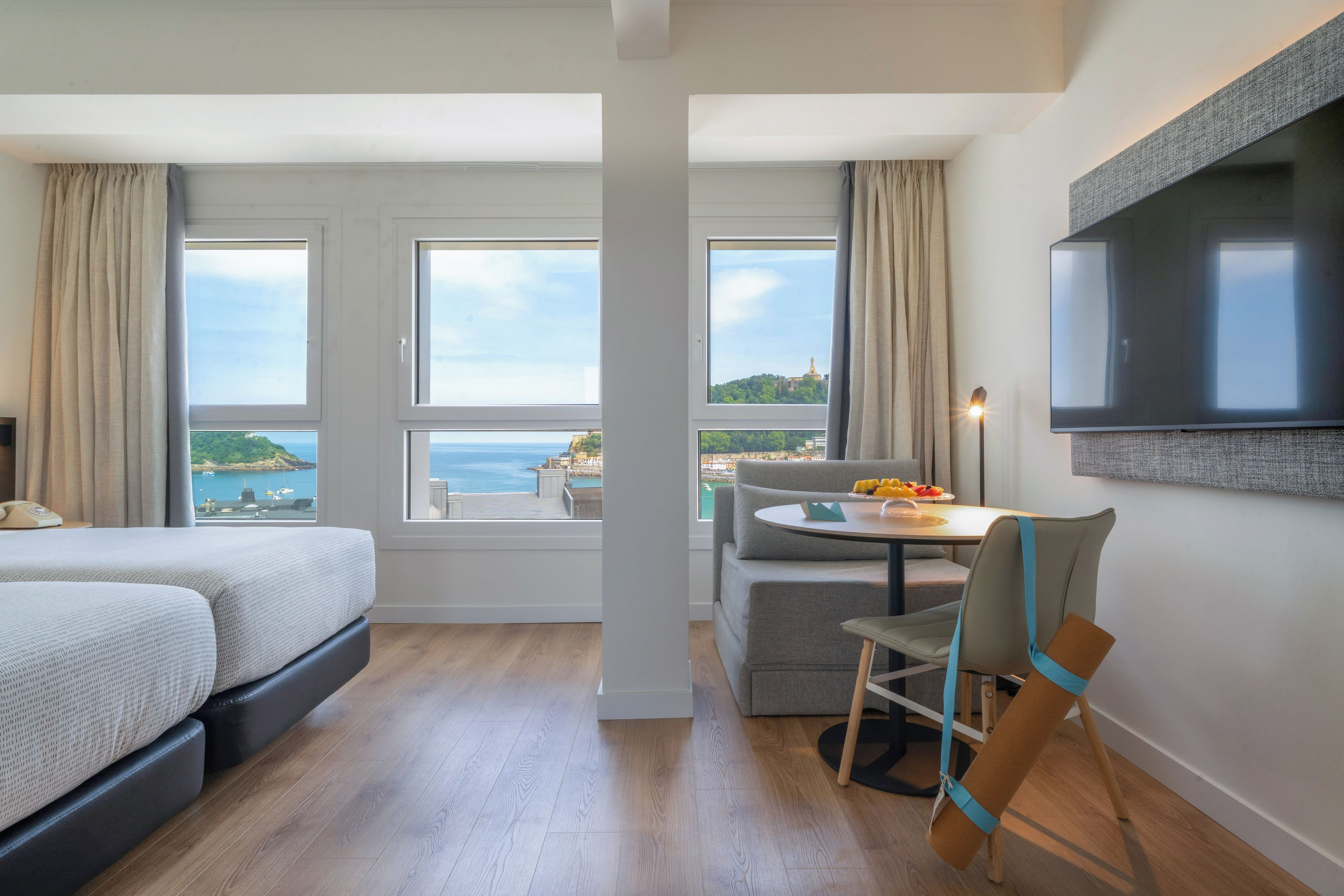 Quarto de hotel com cama, sofá, mesa de jantar e televisão.