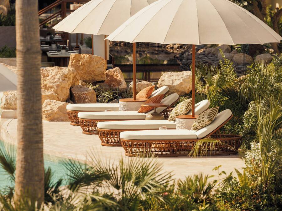 Cadeiras de descanso ao ar livre com guarda-sóis, piscina e vegetação exuberante ao redor.