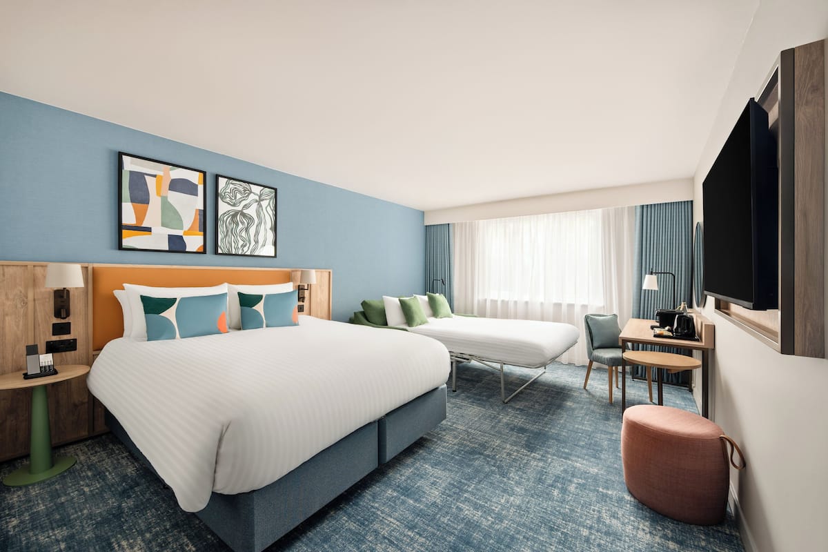 Quarto de hotel com uma cama grande, uma escrivaninha, uma cadeira, uma mesa pequena e uma televisão.