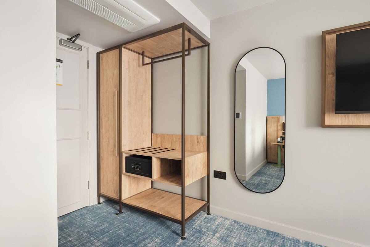 Quarto com guarda-roupa de madeira, espelho e tapete azul.