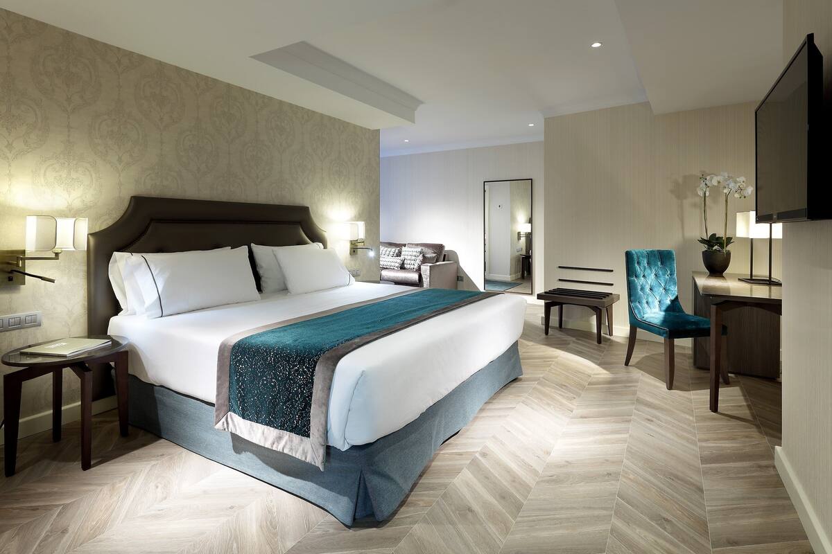 Quarto de hotel com uma cama grande, mesas de cabeceira, uma cadeira, escrivaninha e televisão.