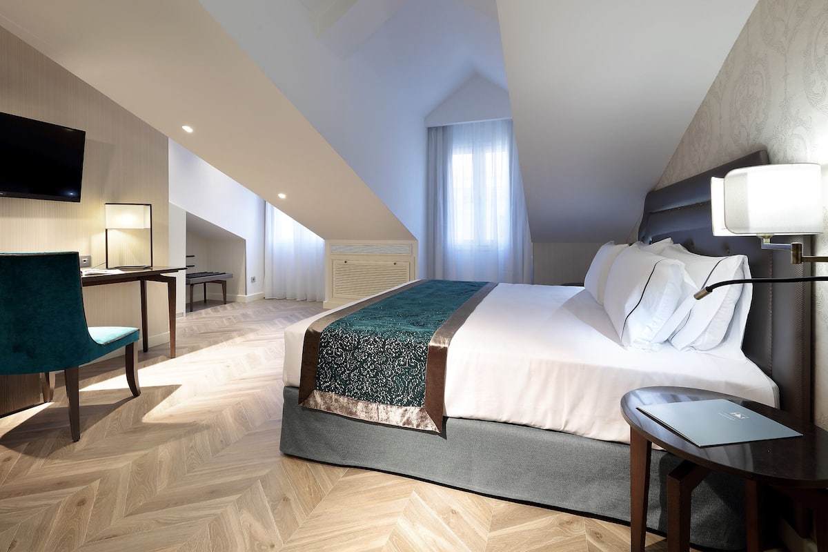 Quarto de hotel moderno com uma cama grande, uma mesa, uma cadeira e uma televisão.
