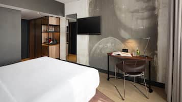 Quarto de hotel com cama, escrivaninha com cadeira, televisão de tela plana e guarda-roupa.